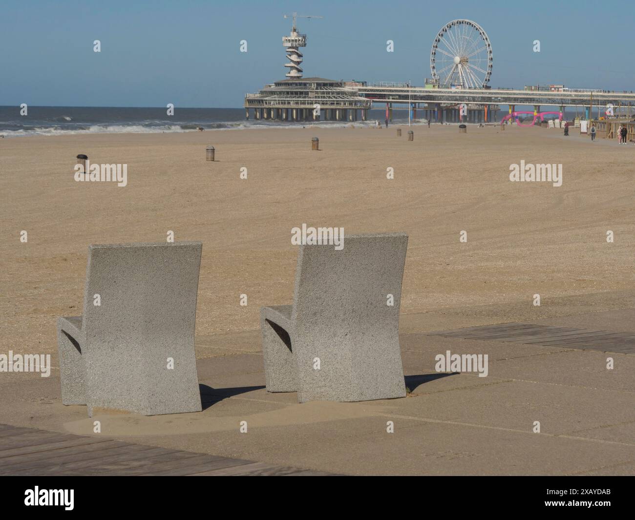 Two chairs on a beach promenade with a view of a pier and a Ferris ...