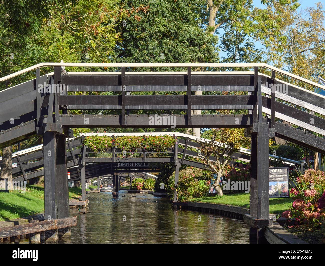 Wooden bridges span a peaceful waterway, flanked by green trees and sky ...