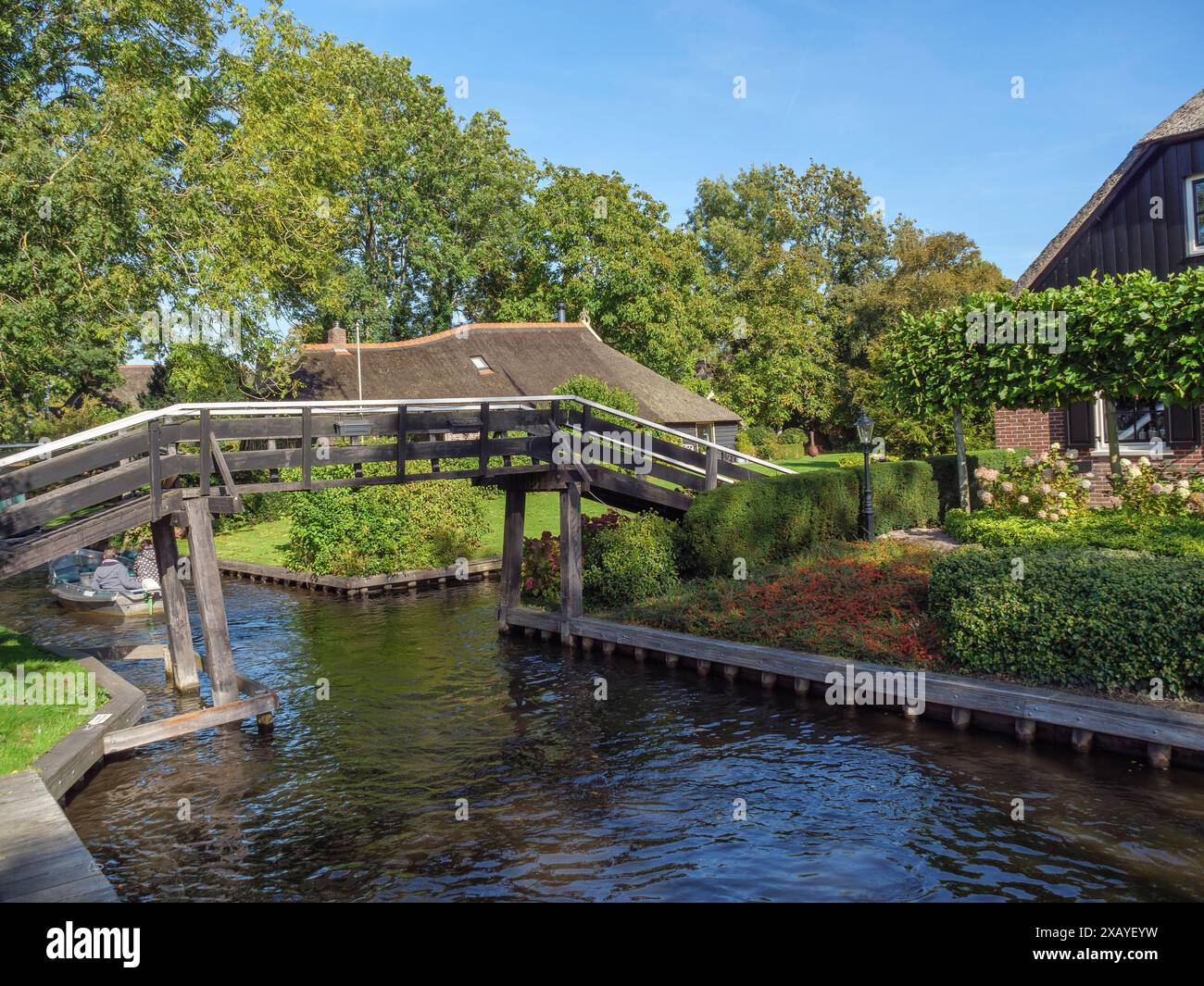 Wooden bridge over a peaceful canal next to a house with a thatched ...