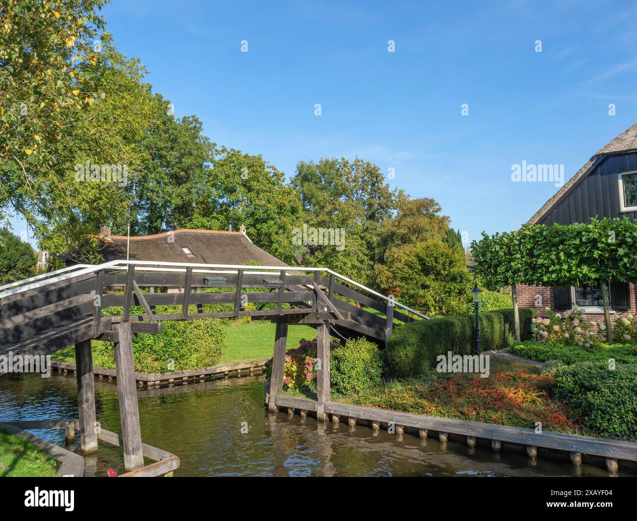 Wooden bridge over a quiet canal surrounded by lush vegetation and a ...
