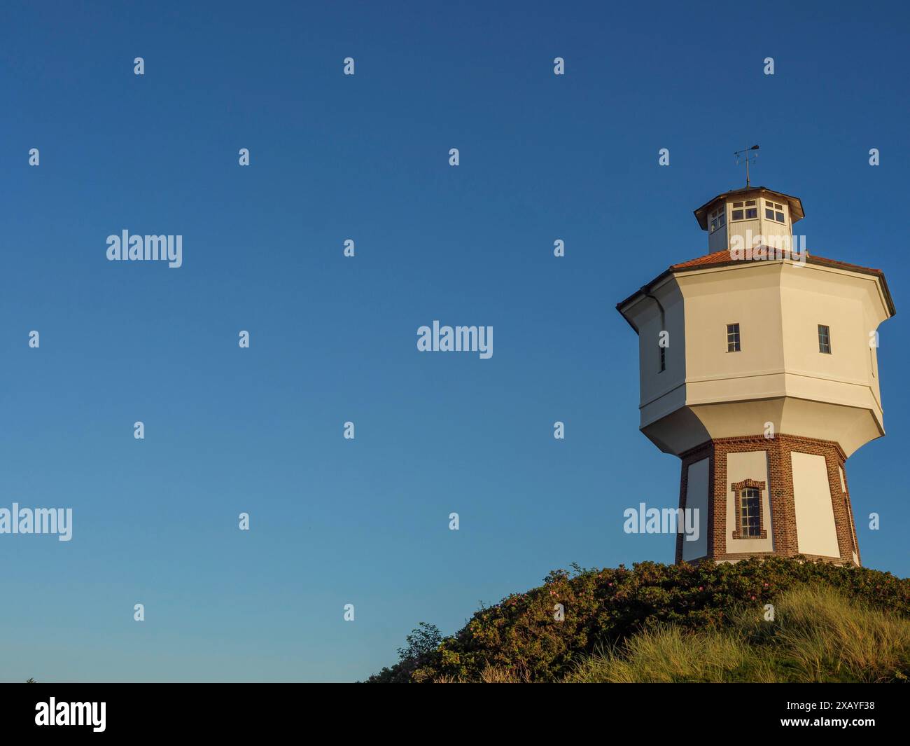 A white lighthouse with a red roof on a hill under a clear sky later in ...
