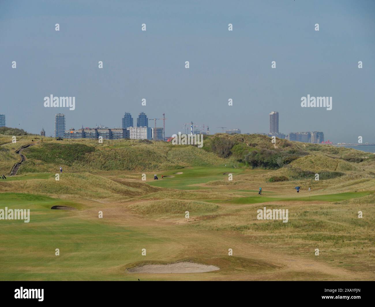 A golf course surrounded by green hills, behind it a city with several ...