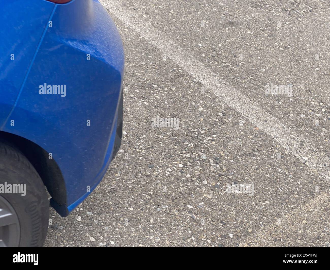 Blue car is parked slightly askew next to a faded white parking line in ...