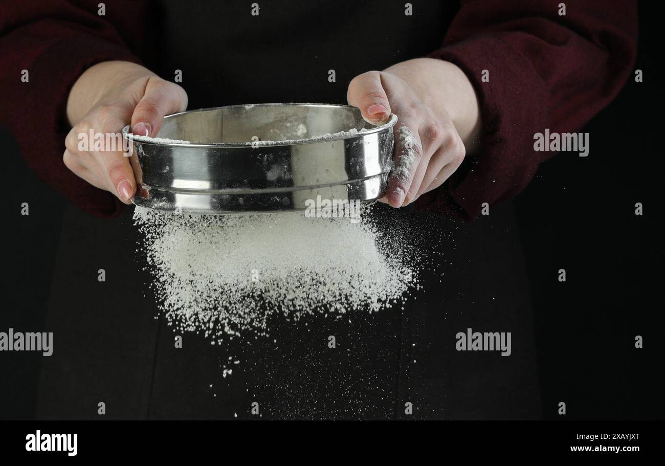 Woman sieving flour at table against black background, closeup Stock ...