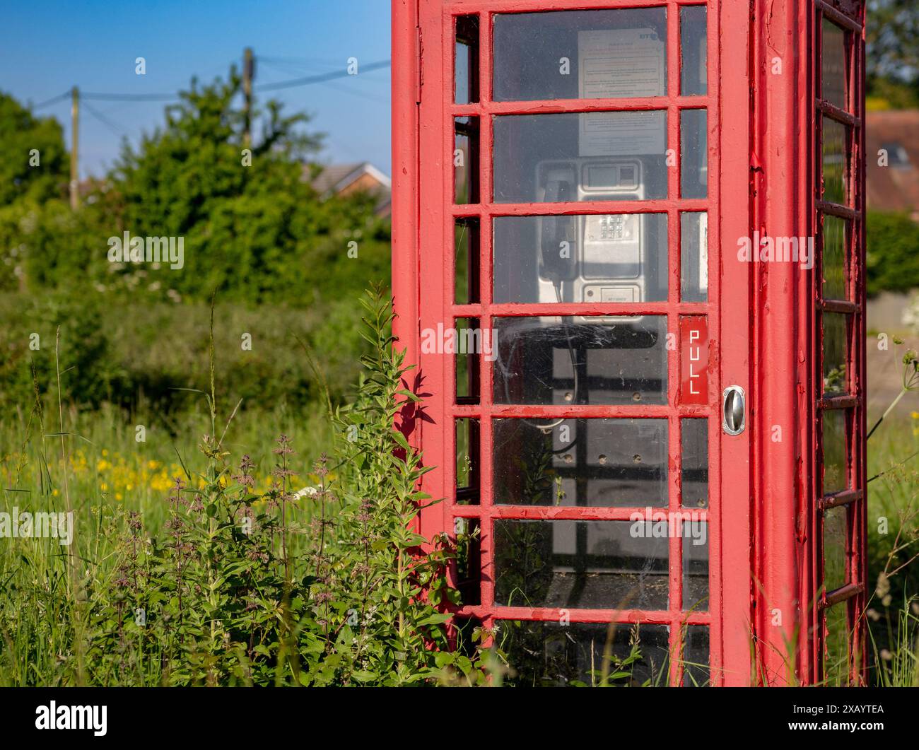 Vintage red British telephone box in a rural setting with greenery and ...