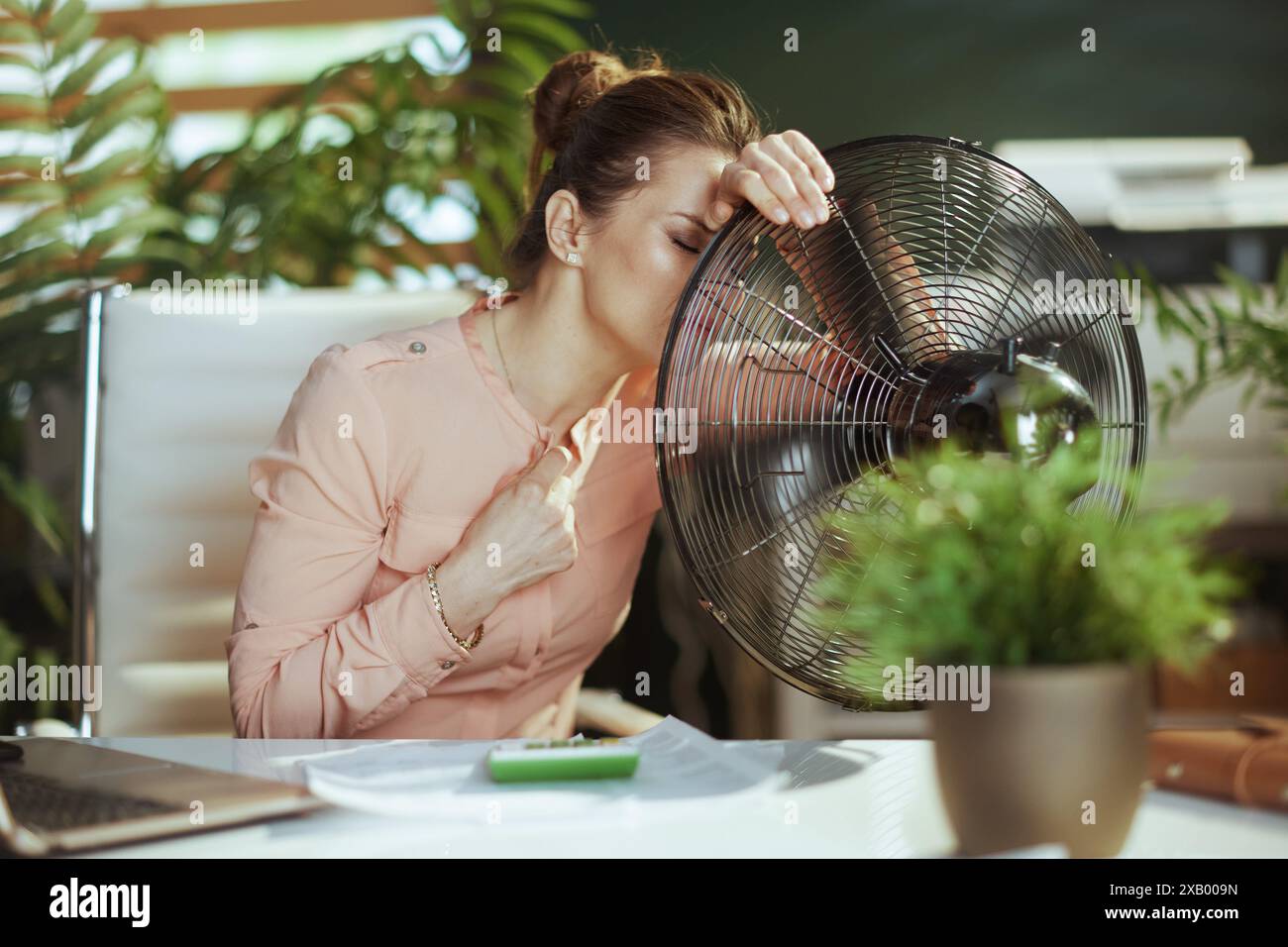Sustainable workplace. modern woman worker at work with electric fan ...