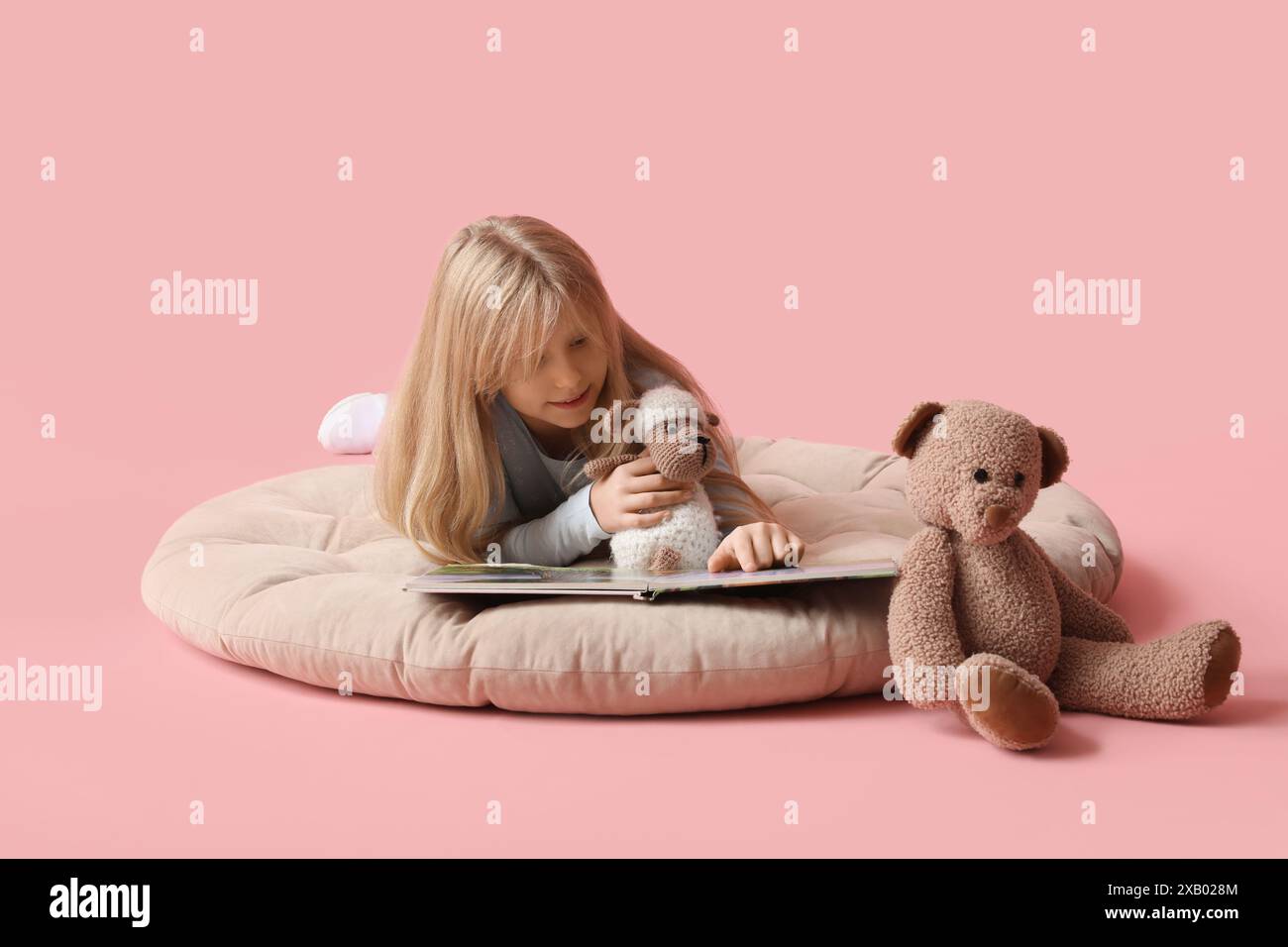 Cute little girl with plush toys reading book on pink background Stock ...