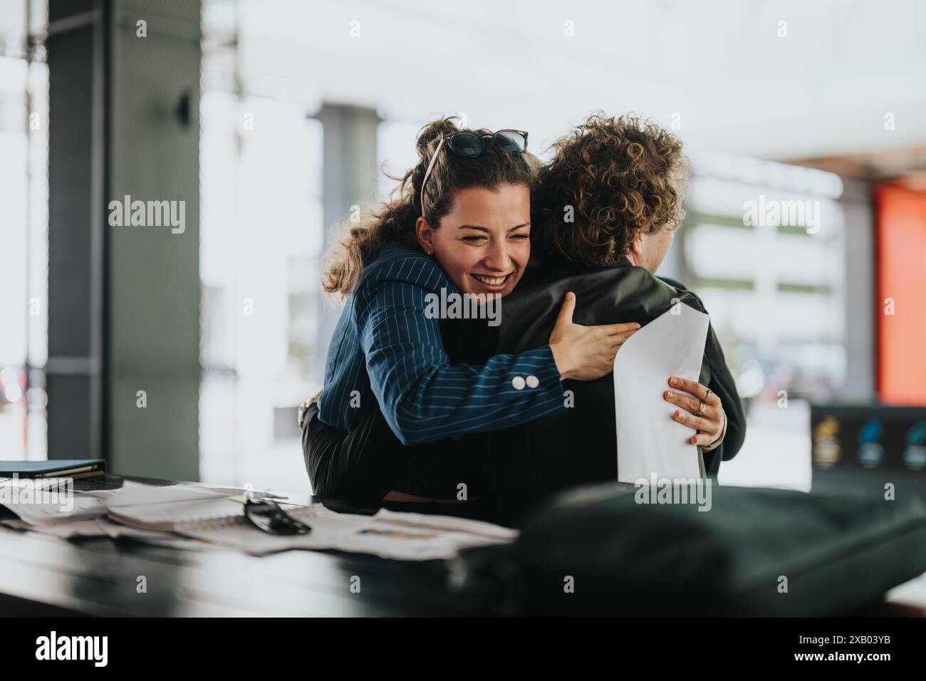 Business colleagues sharing a warm hug in a modern office environment ...