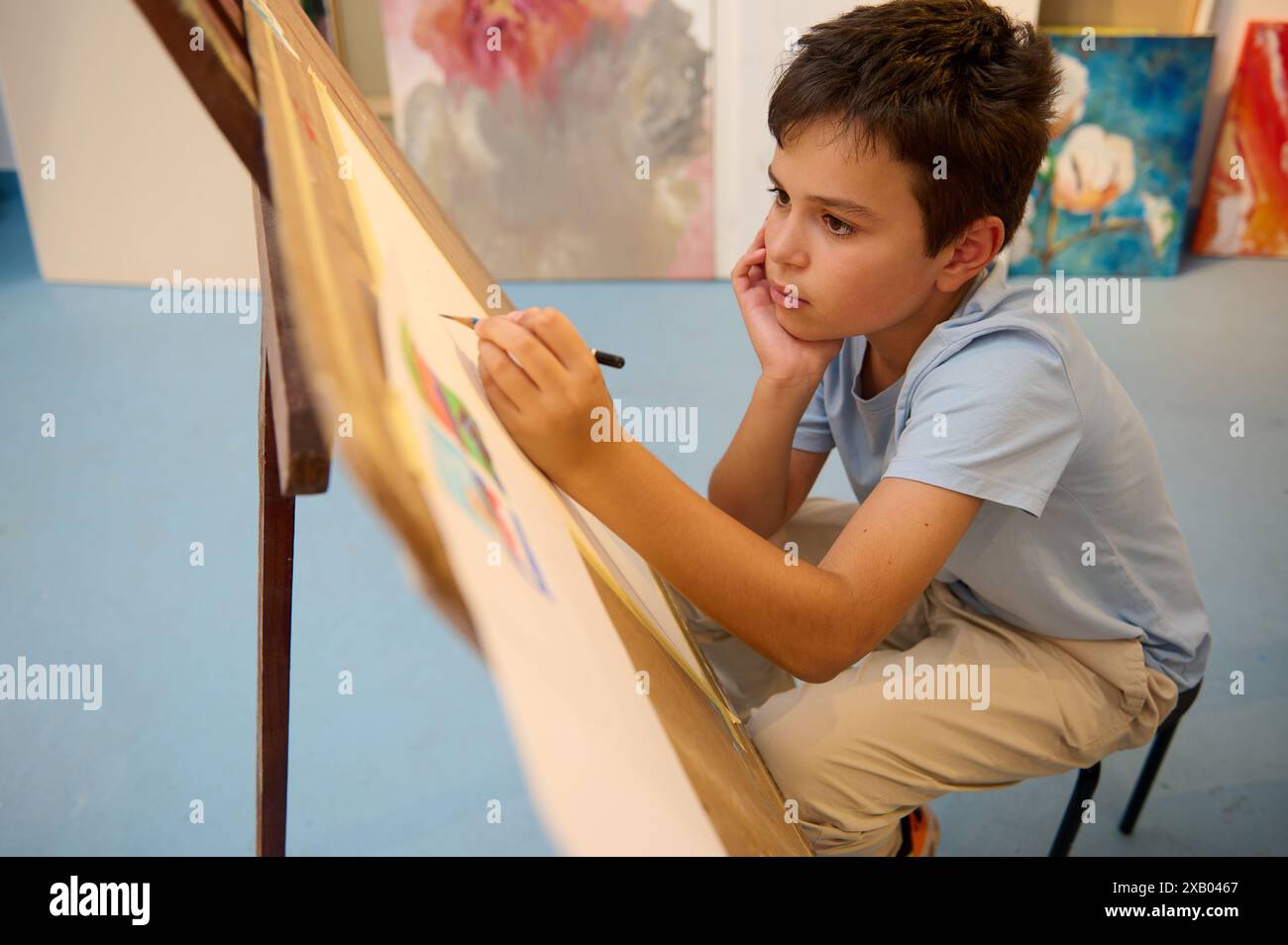Kids have art class, drawing, painting with teacher in workshop. Young boy is deeply focused on ...