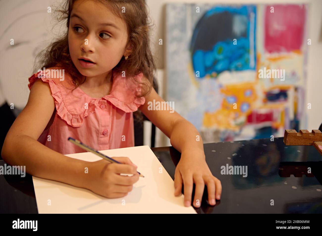 A young girl in a pink dress concentrating on her art class as she ...