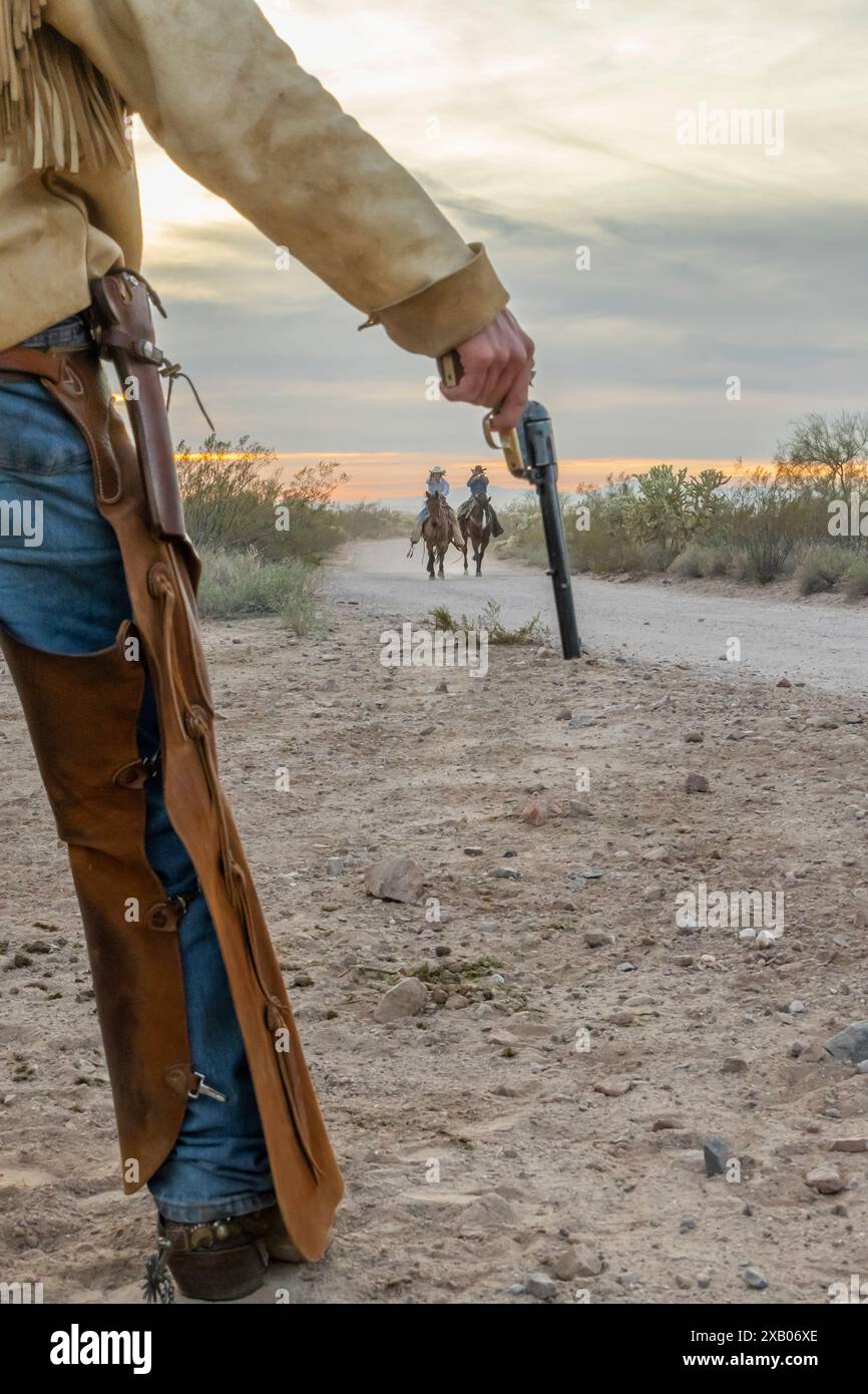 Cowboy holding a revolver while others ride toward him pointing guns ...