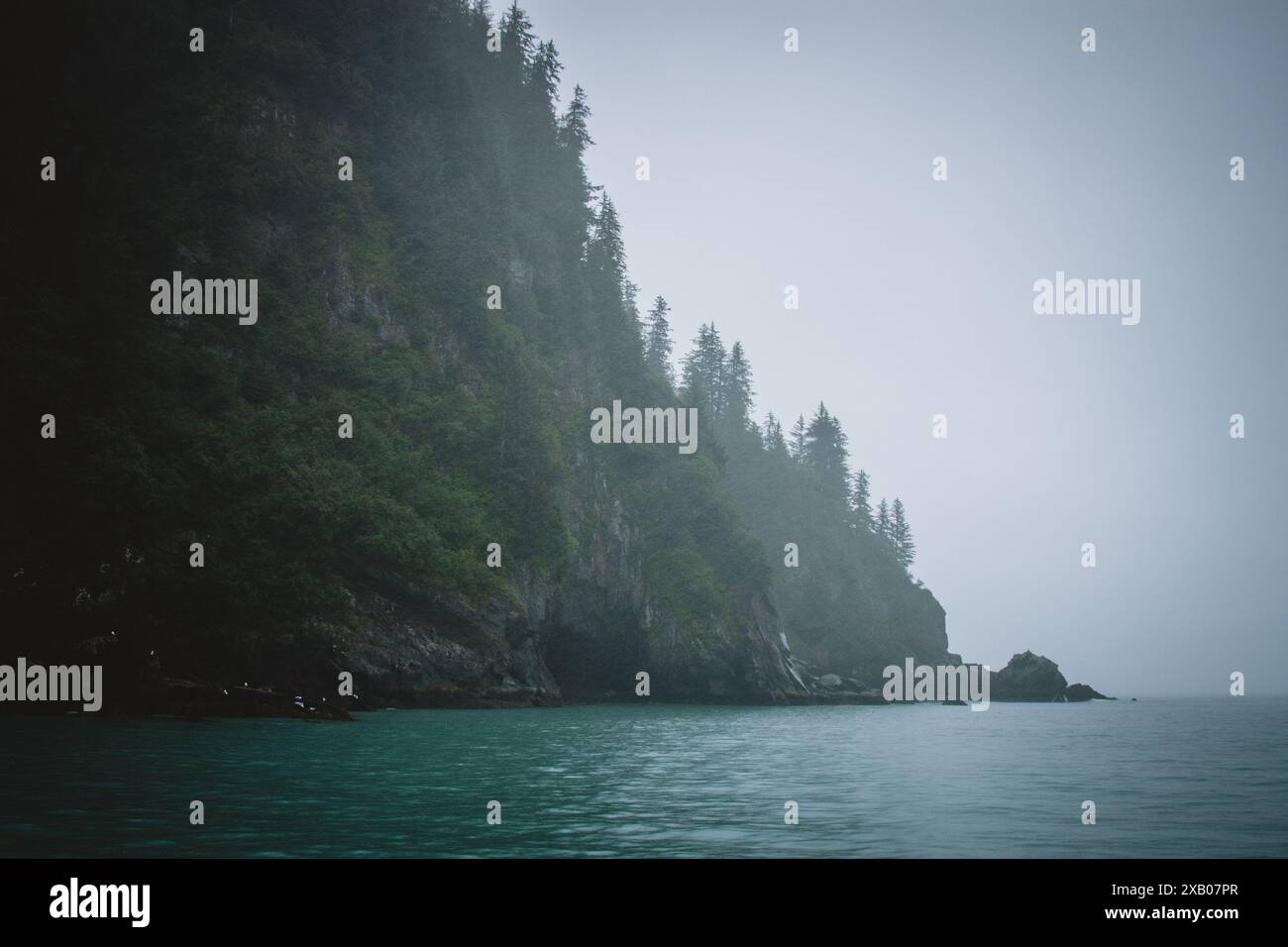 A tranquil scene of the foggy Alaskan coastline, where towering cliffs ...