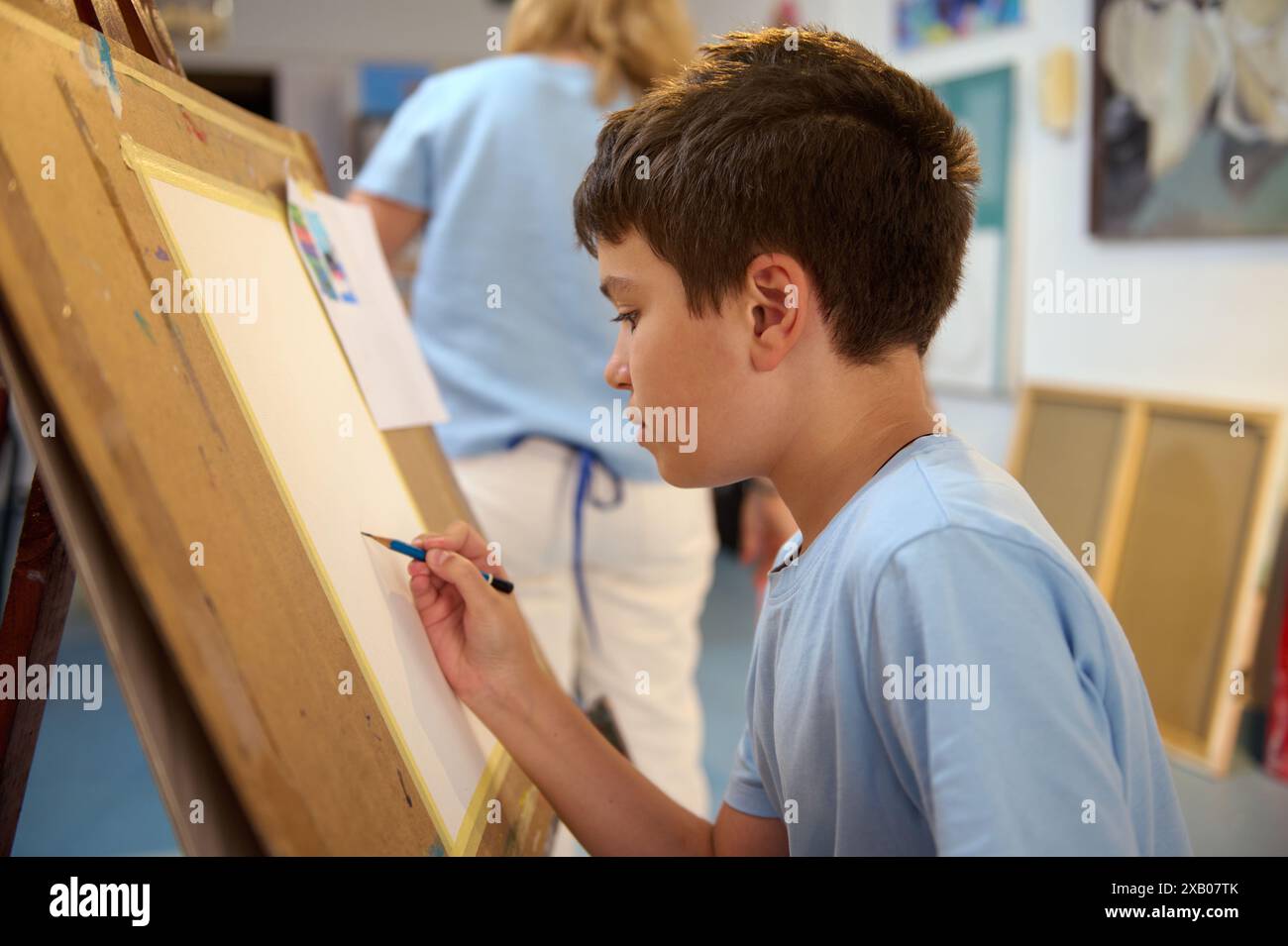 Young boy concentrating on his drawing during an art class, guided by a teacher in a workshop ...