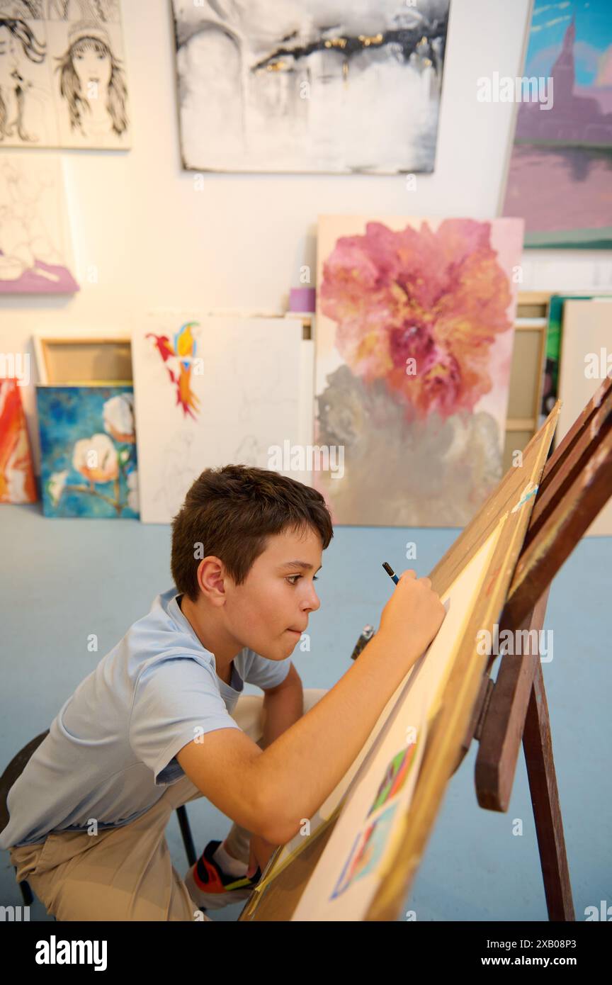 Boy drawing at art class with paintings in background Stock Photo - Alamy