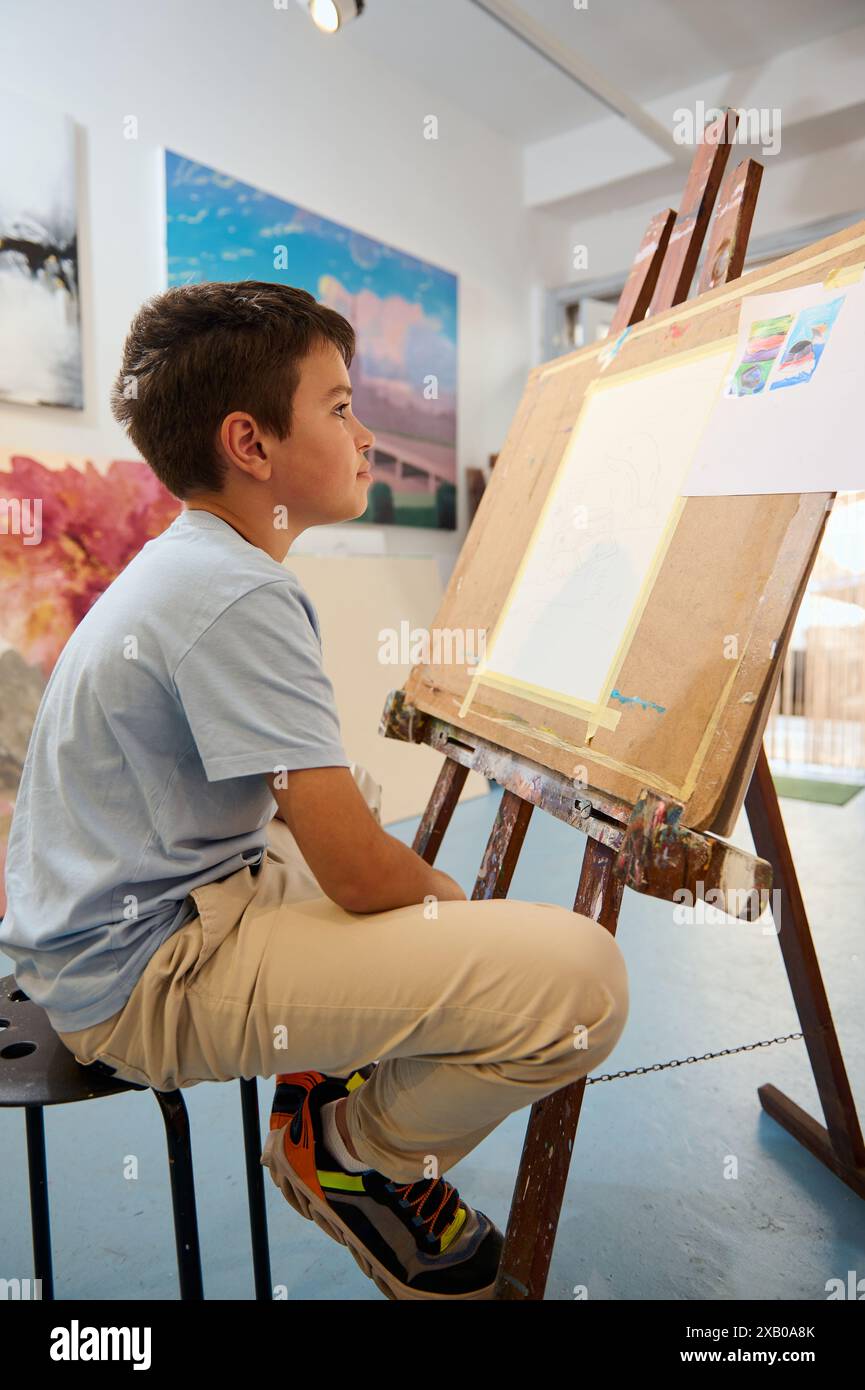 Young boy engaged in art class, drawing and painting on easel in a ...
