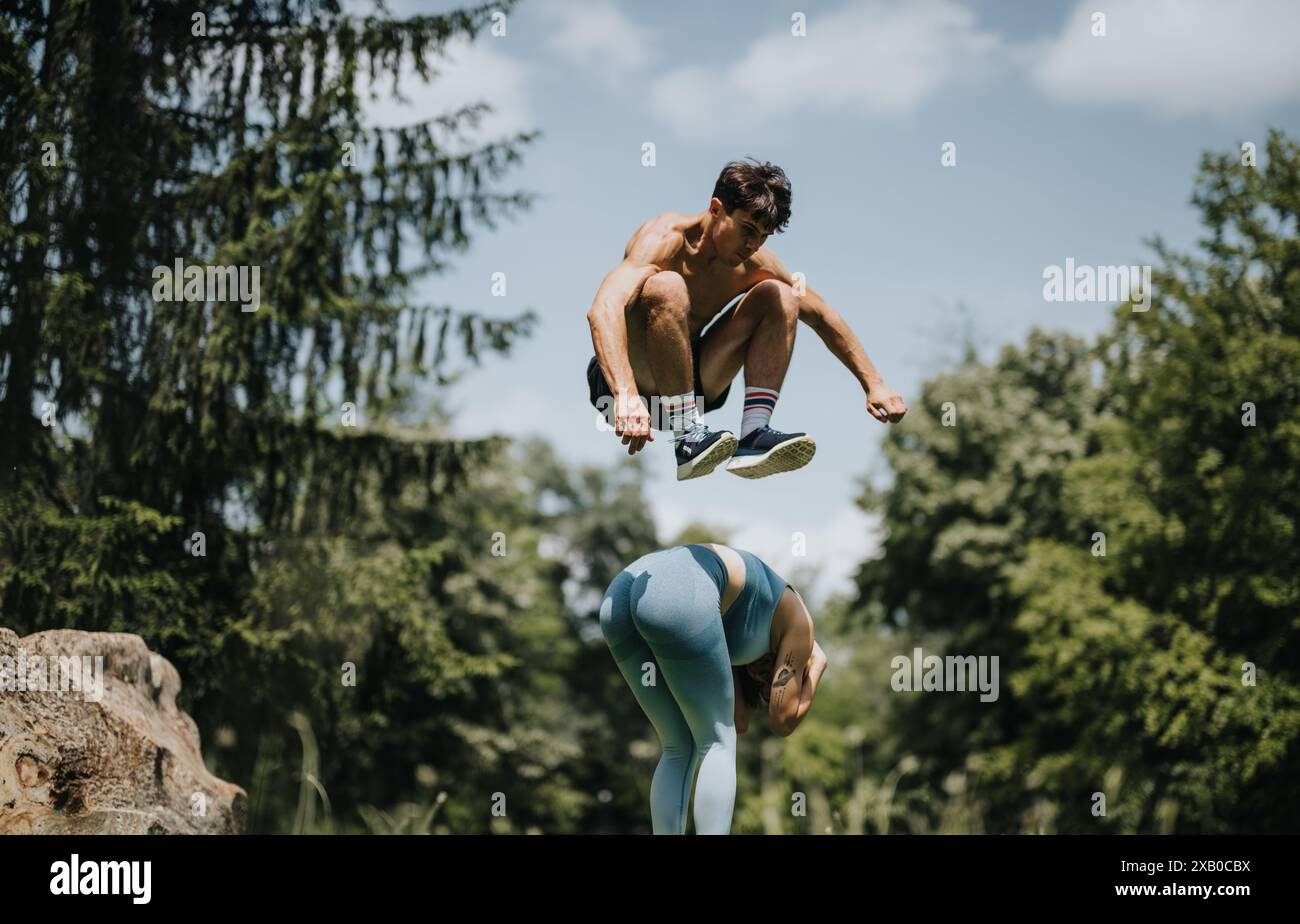 Sports man performing dynamic jump over female friend in an outdoor ...