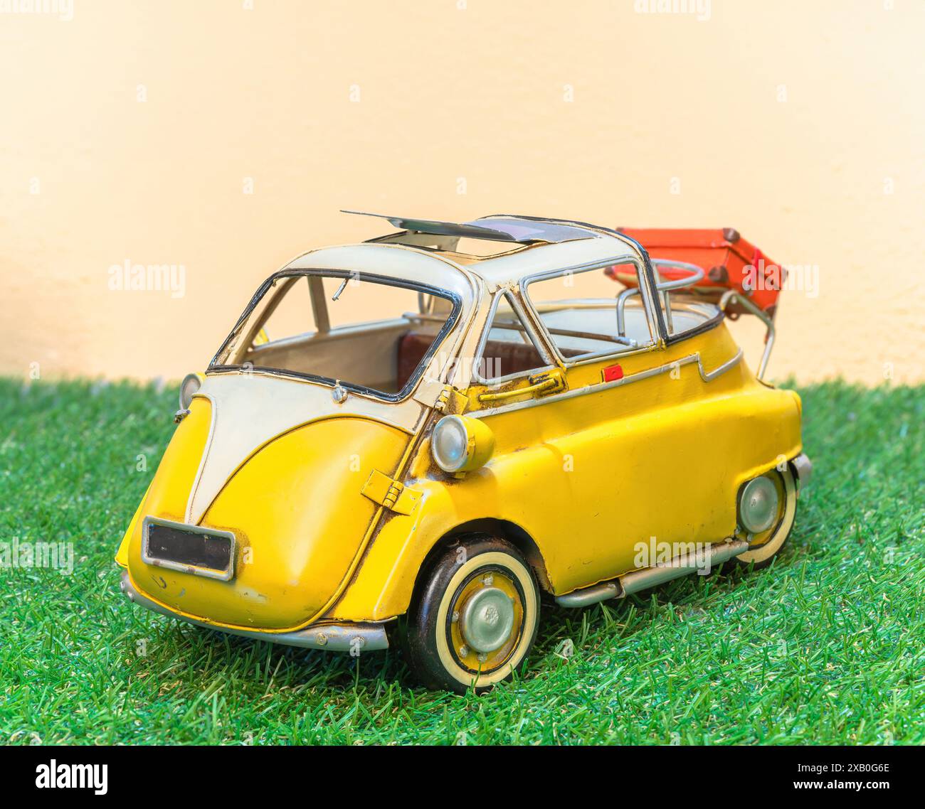 A vintage toy replica depicting a yellow retro microcar with a sunroof ...