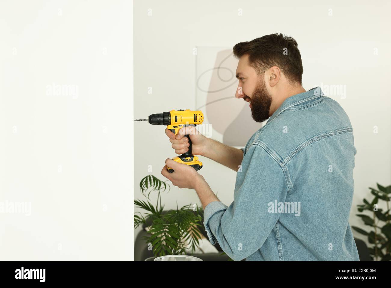 Smiling man working with drill and wall at home Stock Photo - Alamy