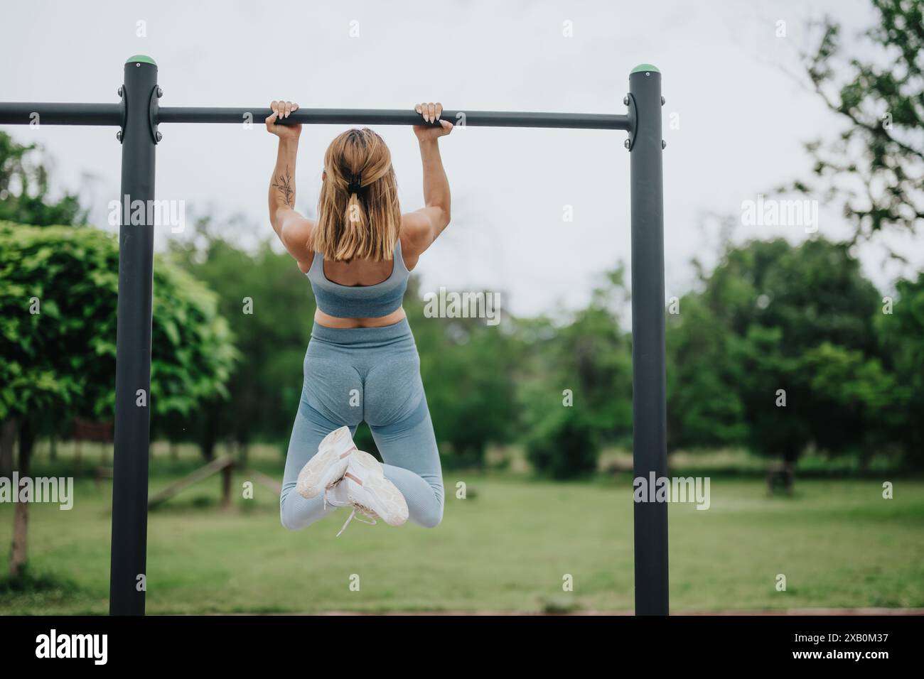 Woman performing pull ups outdoors, exercising biceps and shoulders in ...