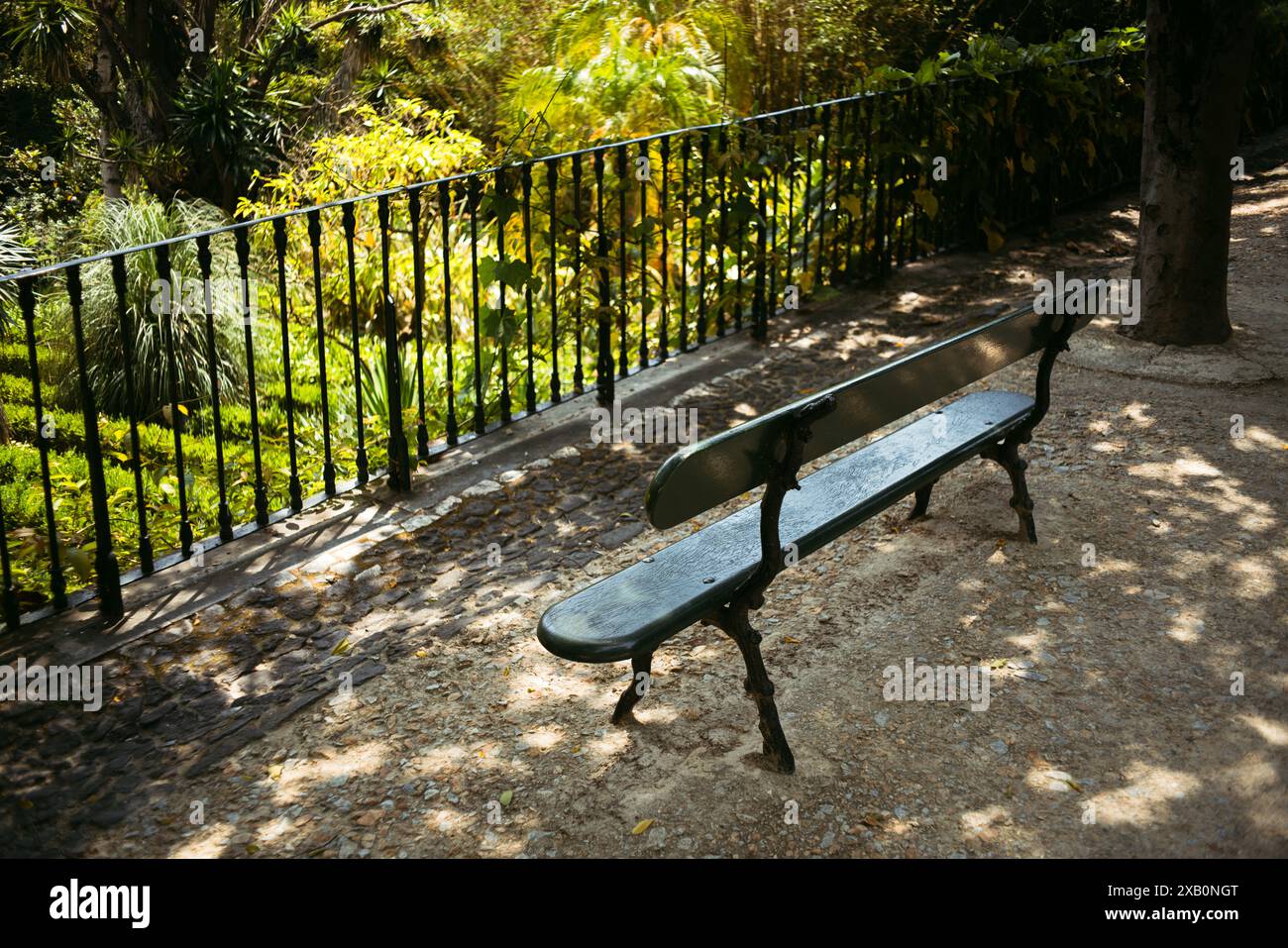 A solitary green park bench in a shaded area near a wrought iron fence ...