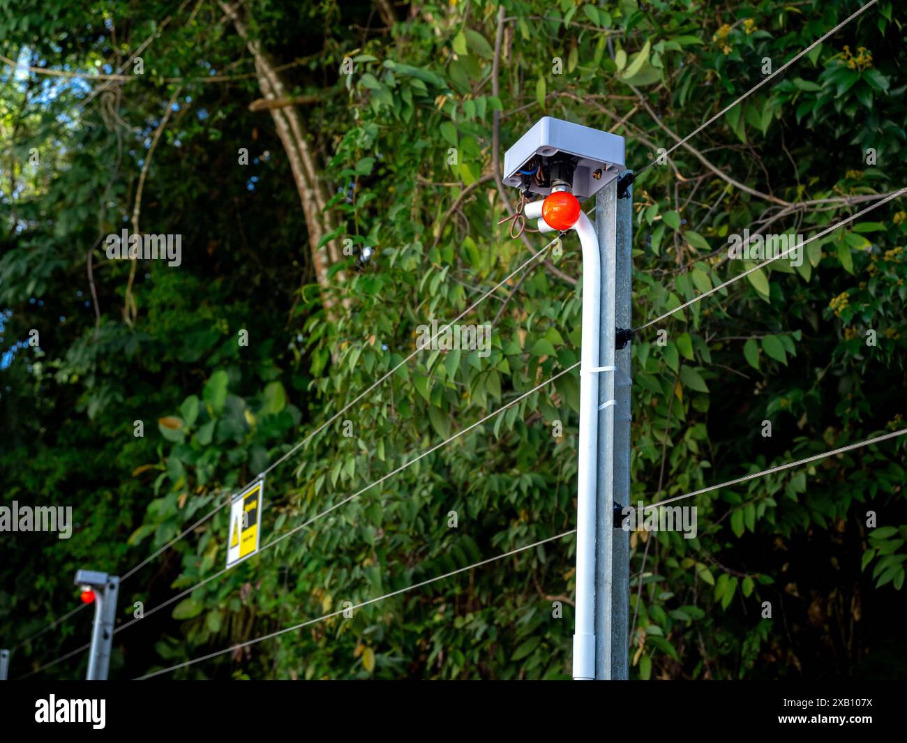 Red light bulb on poles near electrical fence warning sign with ...