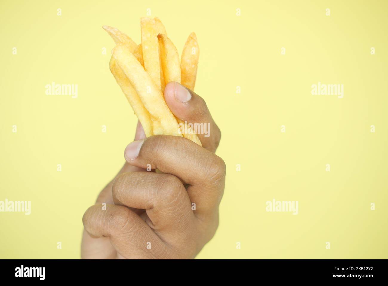 Hand holding French Fries with crispy texture, against a yellow ...