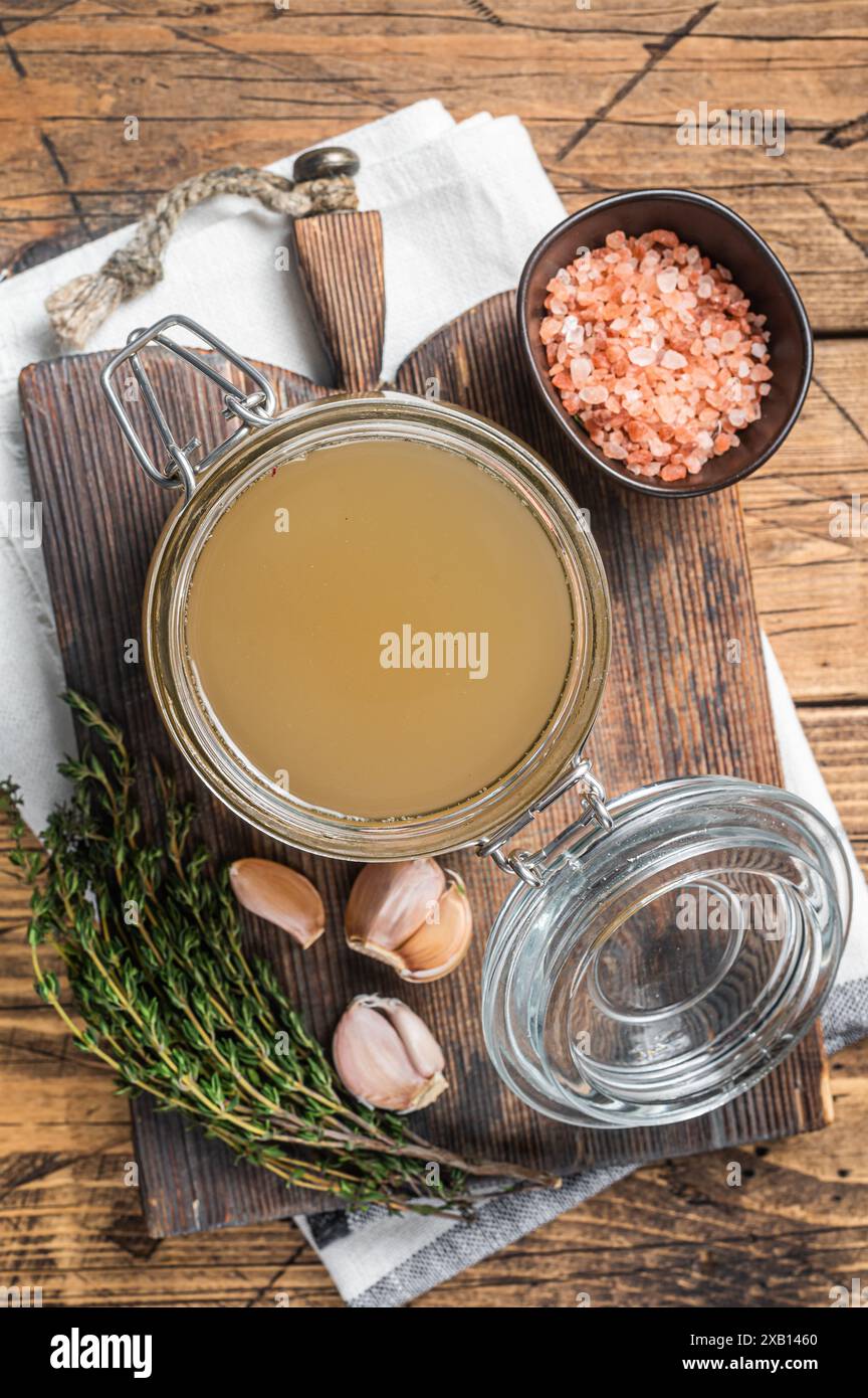 Bone broth for chicken soup in a glass jar. Wooden background. Top view ...
