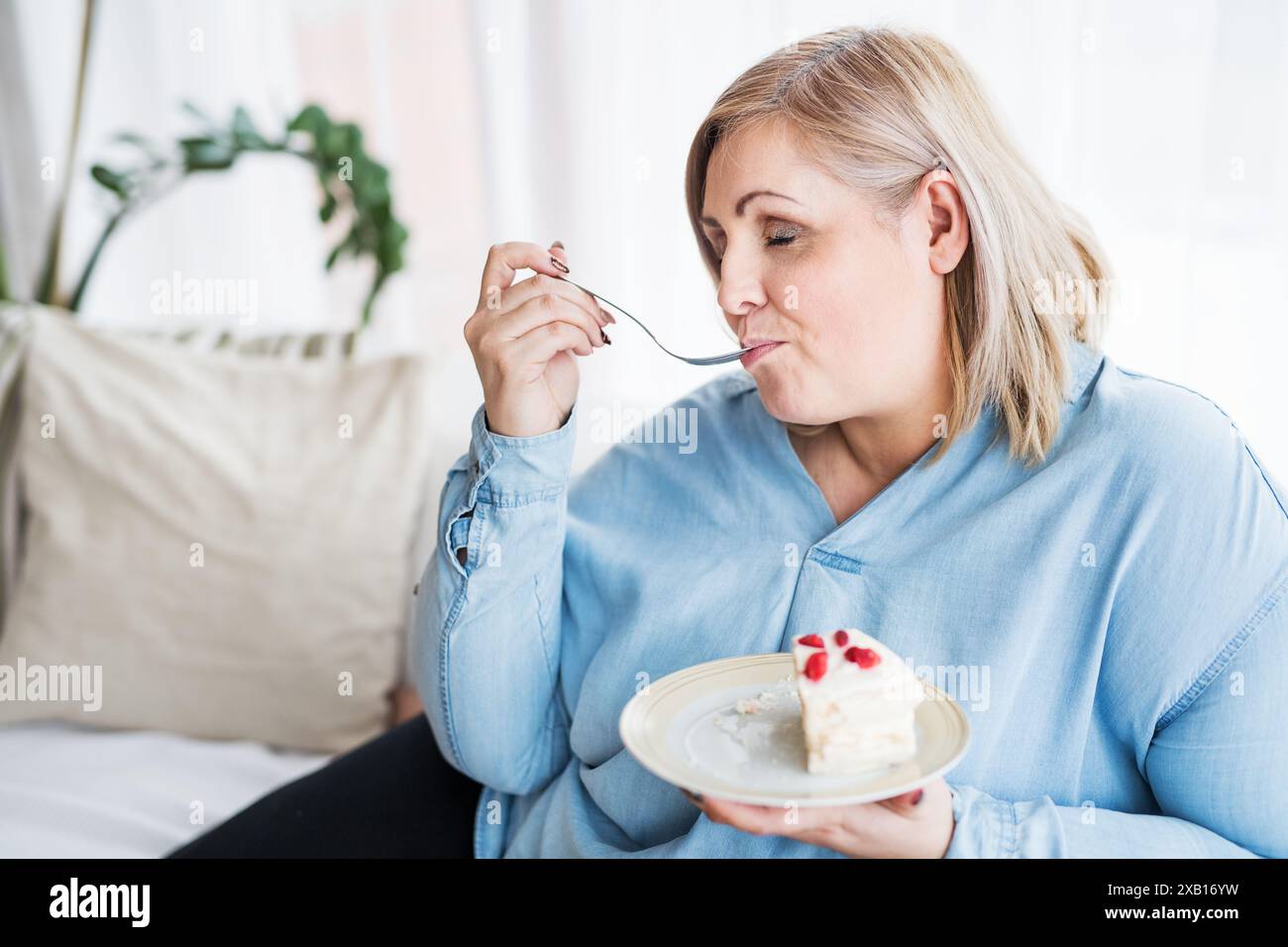 Portrait of beautiful young overweight woman at home, eating slice of ...