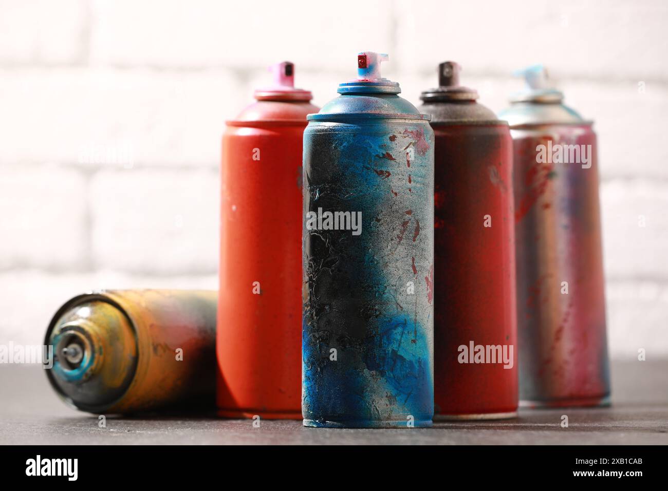 Many spray paint cans on gray surface against white brick wall, closeup ...