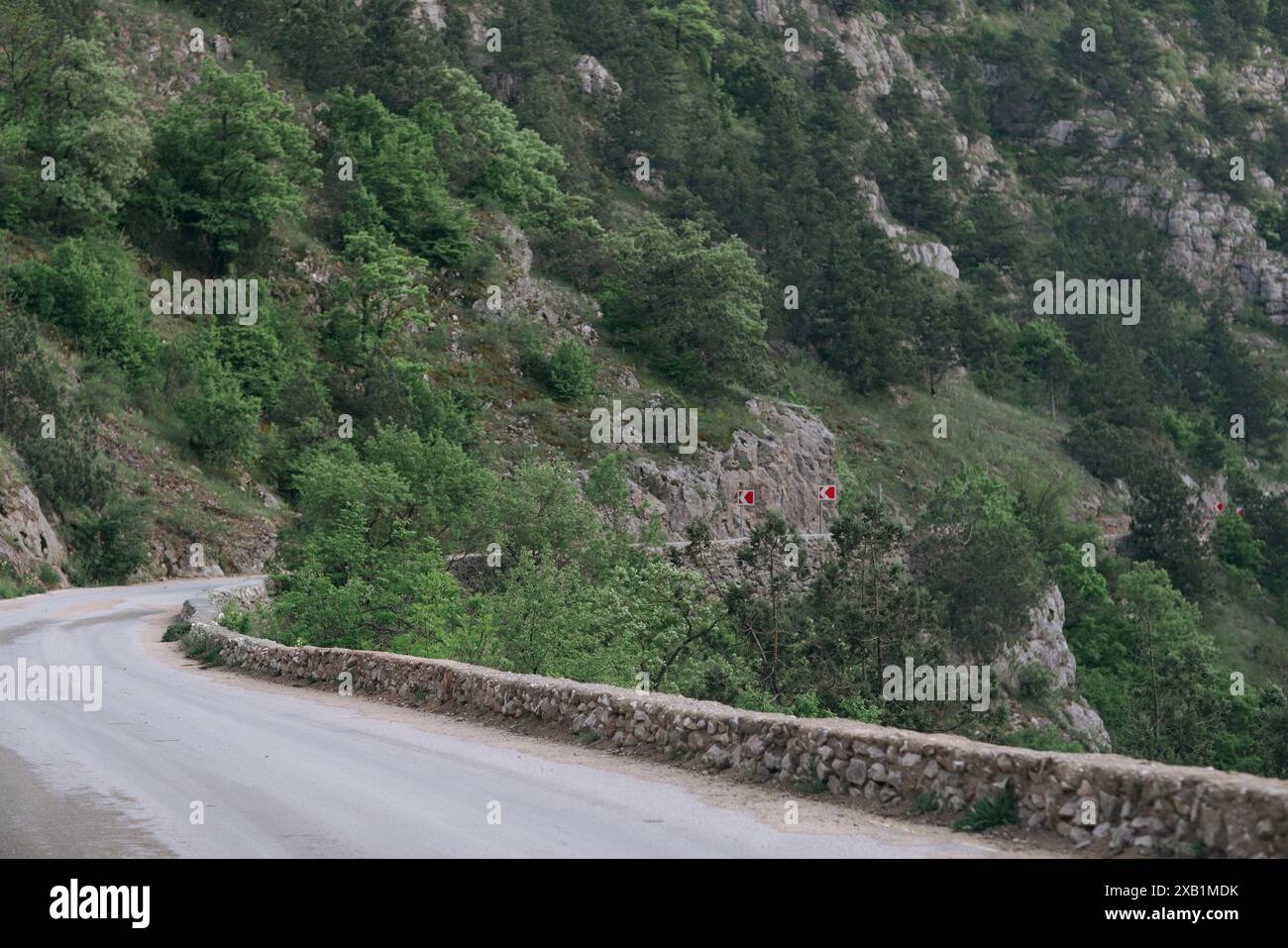 A road with a stone wall on the side and trees in the background. The ...