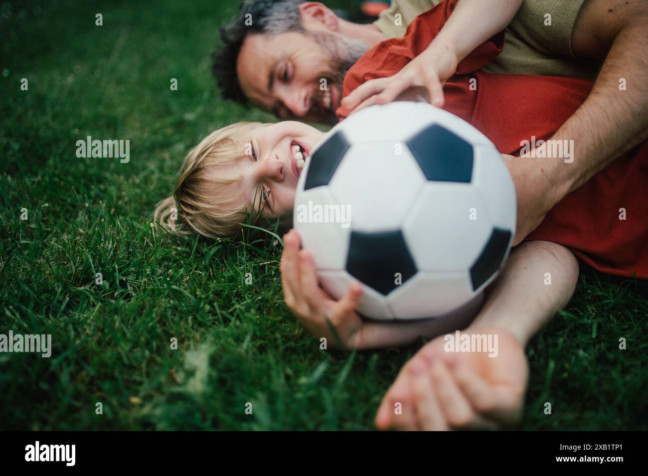 Dad lying on grass with son, laughing and having fun. Father and boy ...