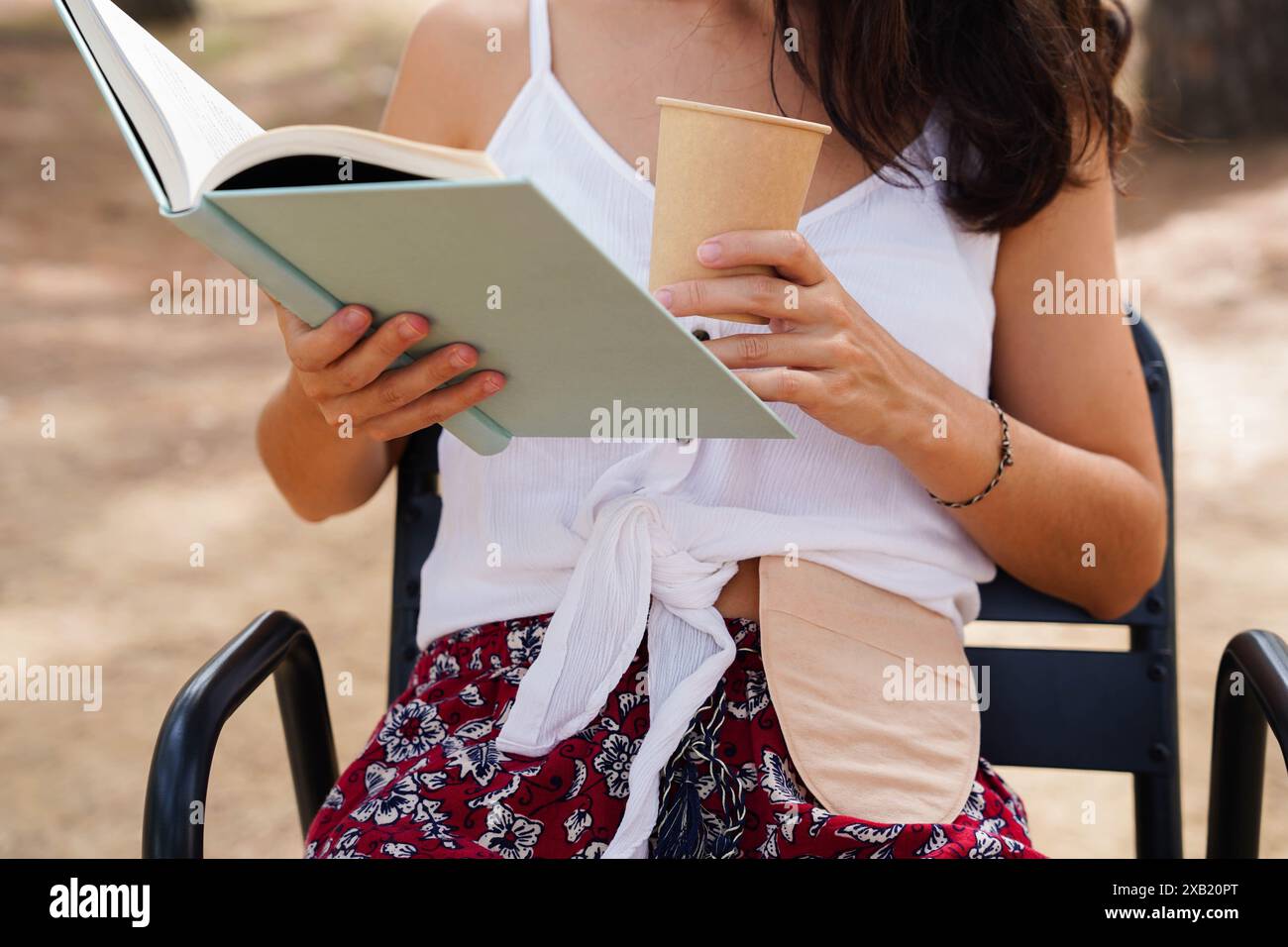 Unrecognizable woman with an ostomy bag drinking and reading a book ...