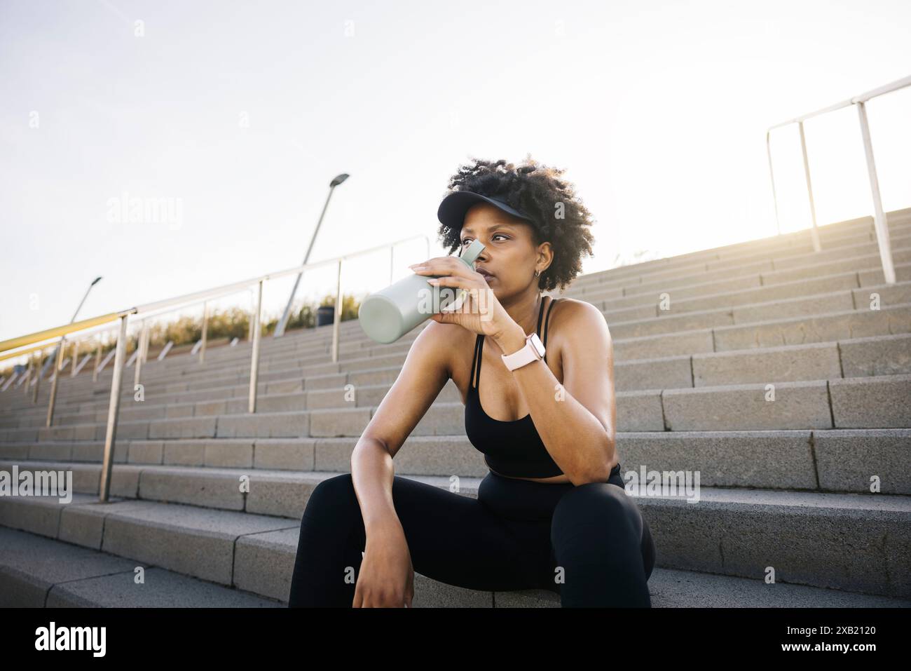 Young woman drinking water from a bottle while resting on the steps ...