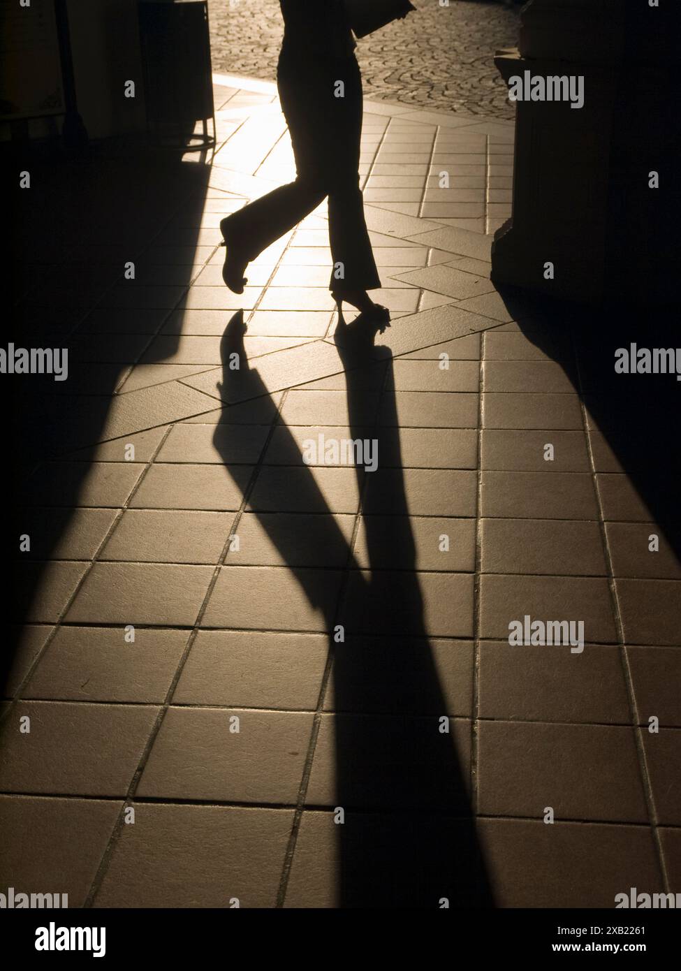 A female pedestrian casts a long shadow on the stone as she walks by in ...