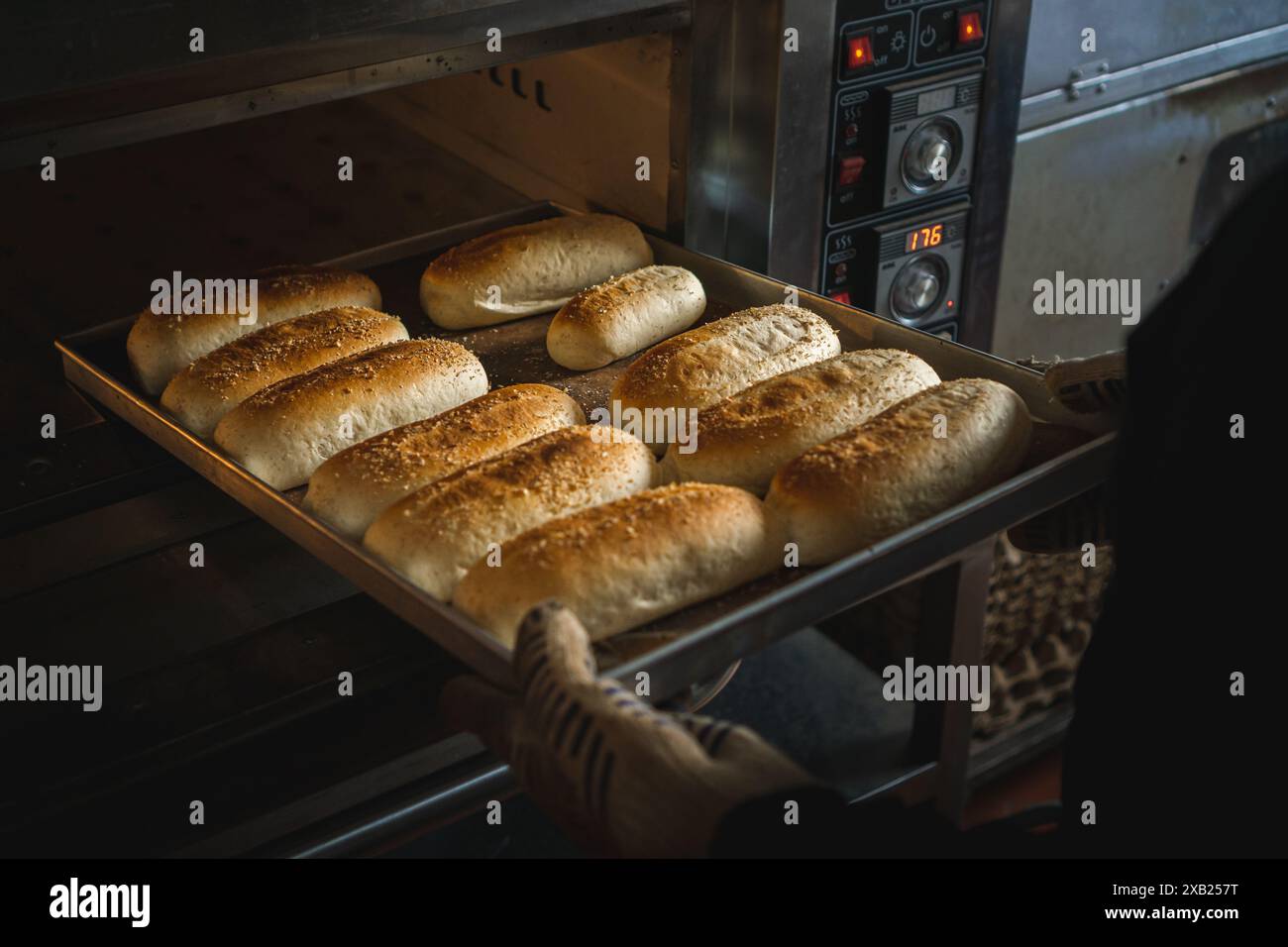 Close up of baker is taking off hotdog bun from oven, small business ...