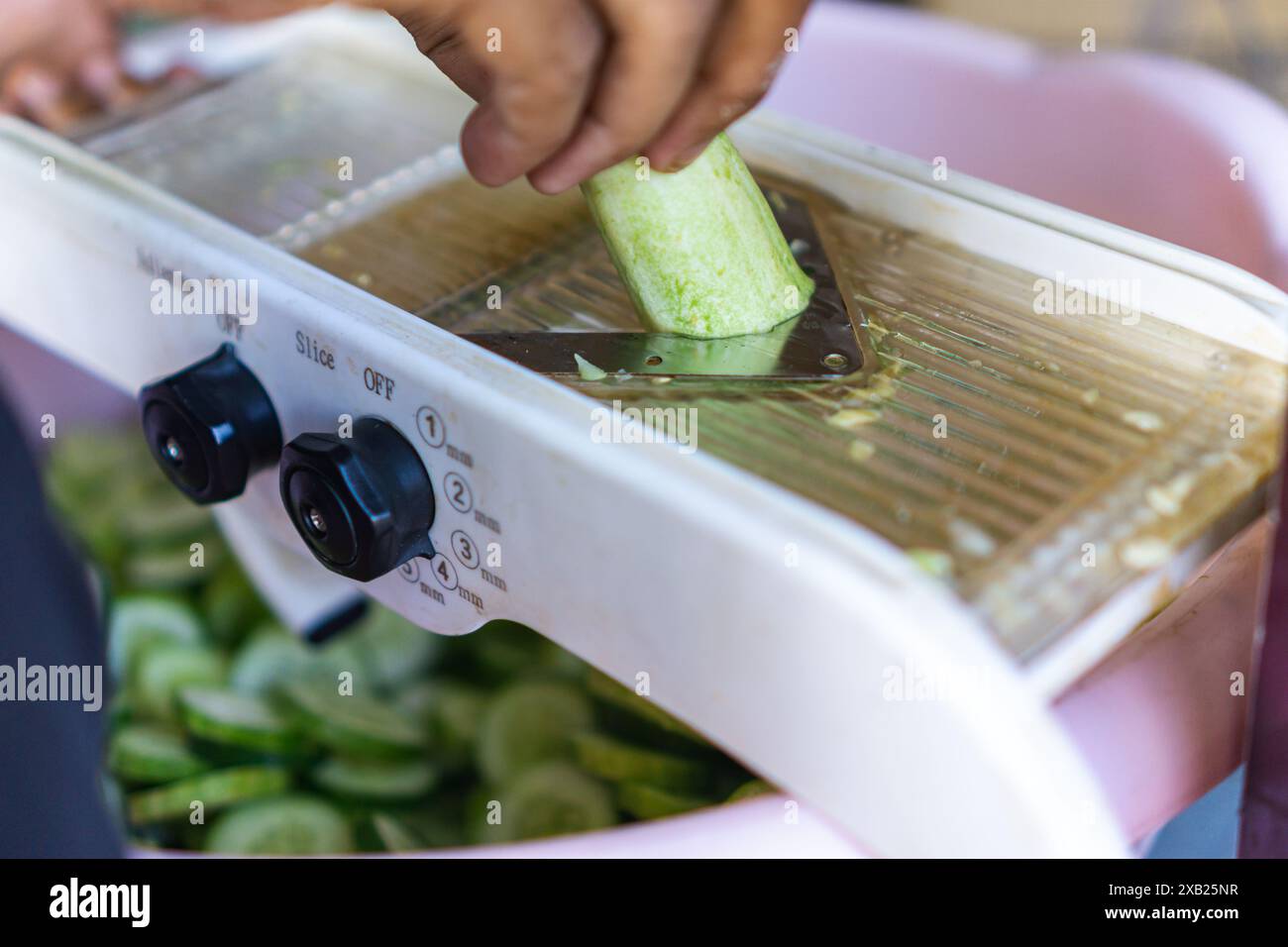 slicing fresh cucumber into thin slice using a mandolin, process of ...