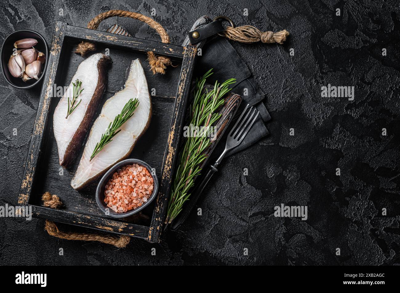 Raw halibut fish steak in wooden tray with herbs. Black background. Top ...