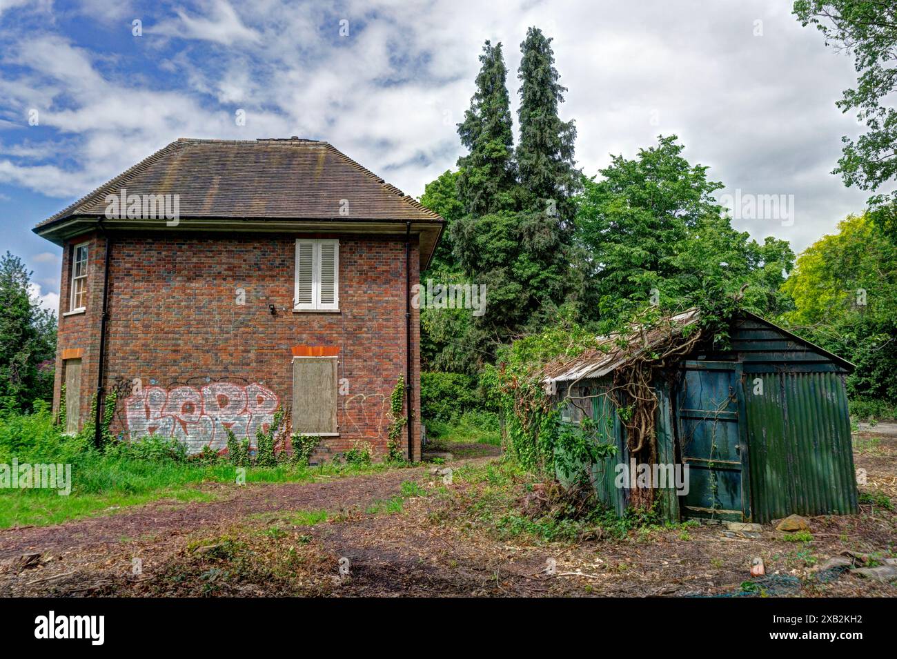derelict red brick house with graffiti and green wooden shed on land ...