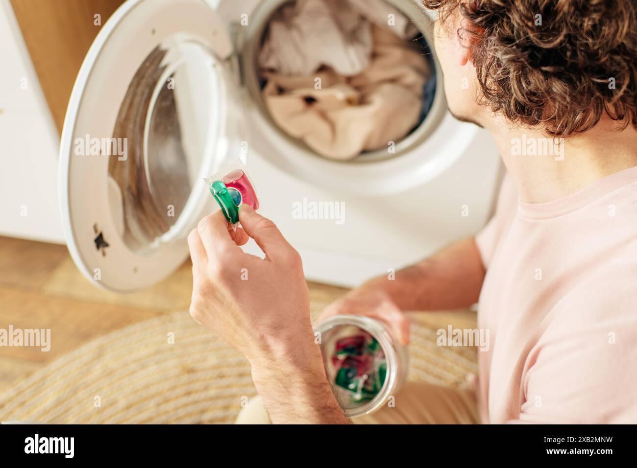 A man in cozy homewear holds a cup of detergent in front of a washing ...