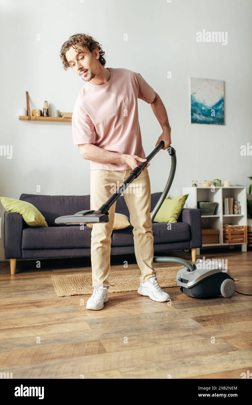 A handsome man in cozy homewear diligently vacuums his living room ...