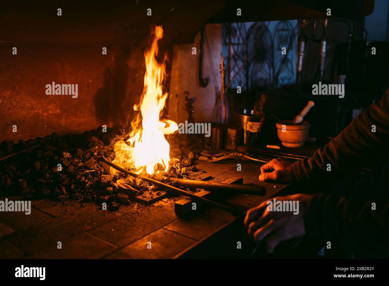 An artisan blacksmith shapes metal on an anvil with a fiery forge in ...