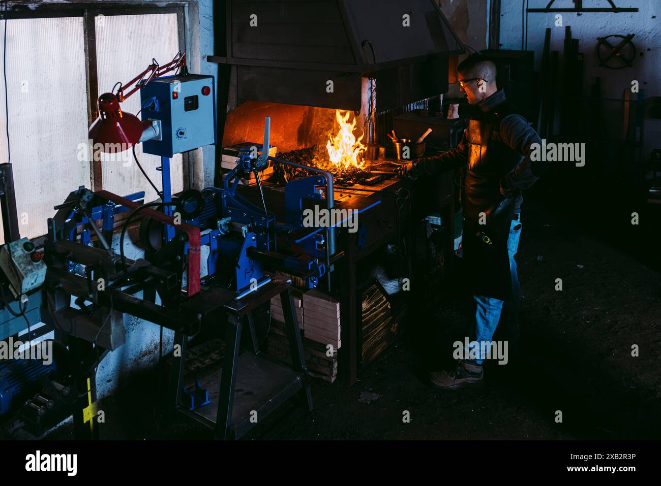 A male blacksmith attentively operates alongside a fiery forge ...