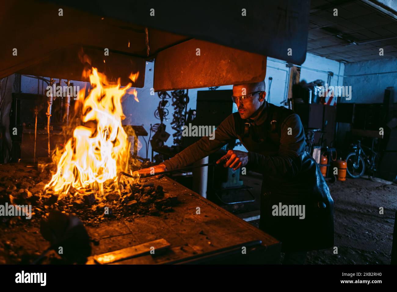 A male blacksmith skillfully works with metal over the fiery forge in a ...