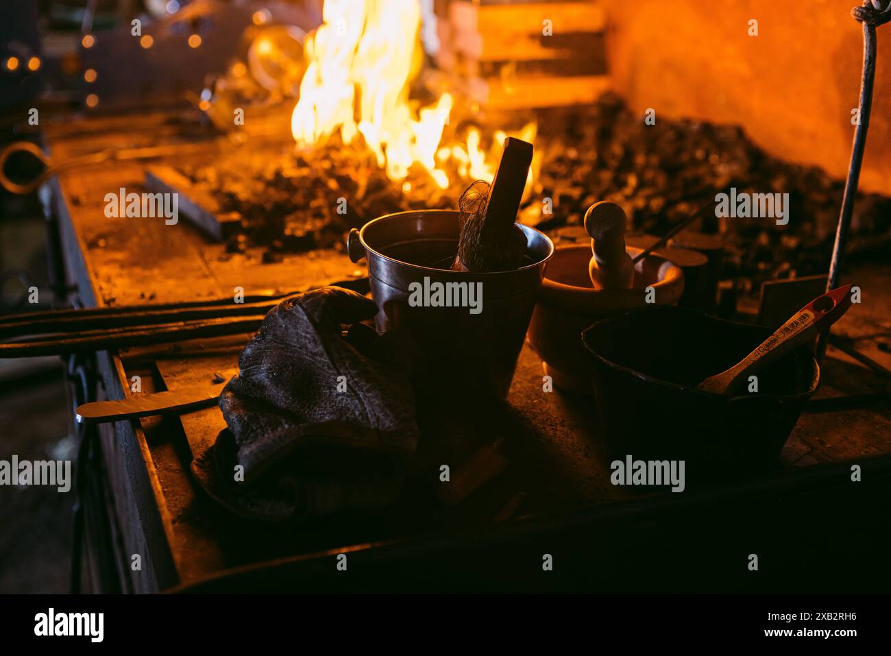 The warm glow of a forge illuminates blacksmithing tools laid out on a ...