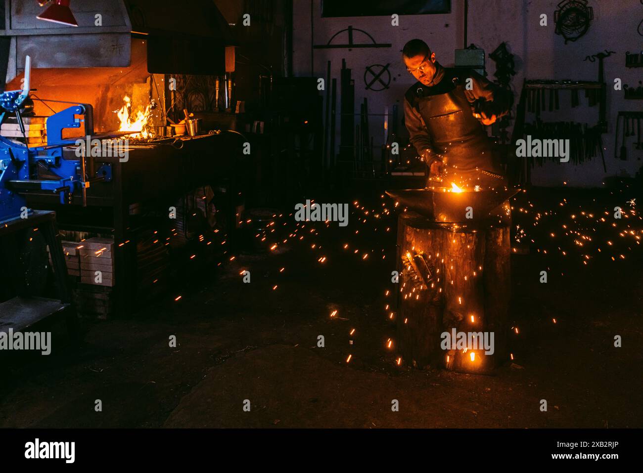 Blacksmith forging hot metal with hammer at anvil in a dark workshop ...