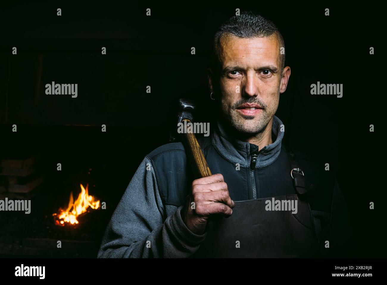 Confident male blacksmith with hammer in a forge standing looking at ...