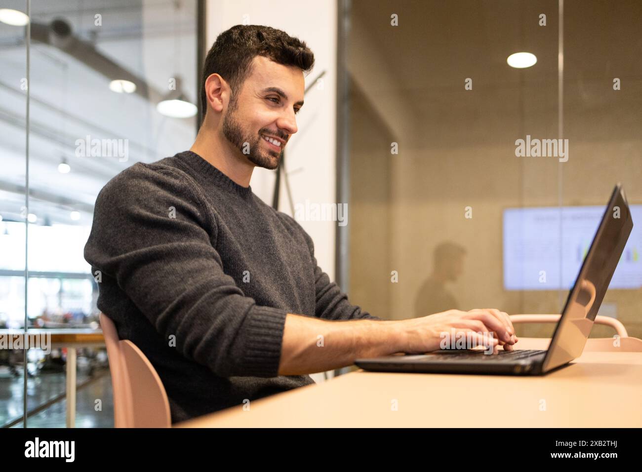 A cheerful young man works diligently on his laptop at a modern ...