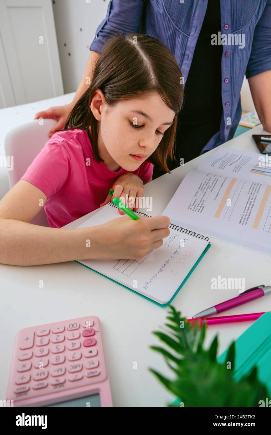 Young girl focusing on homework in a bright room with a calculator and ...