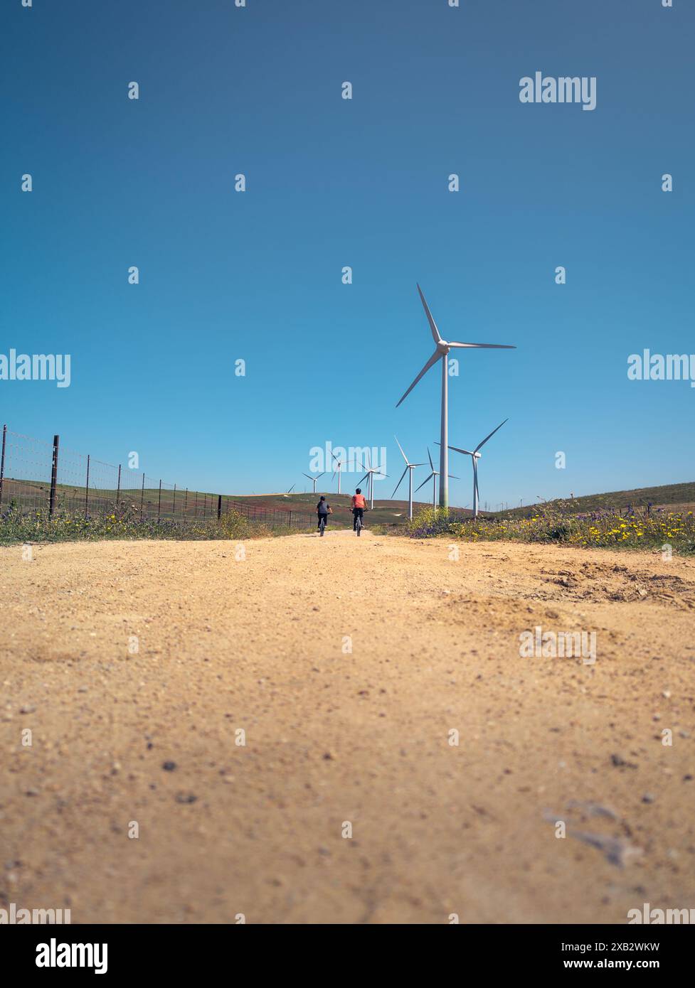 Two people walk toward wind turbines under the blue sky at Atlanterra ...