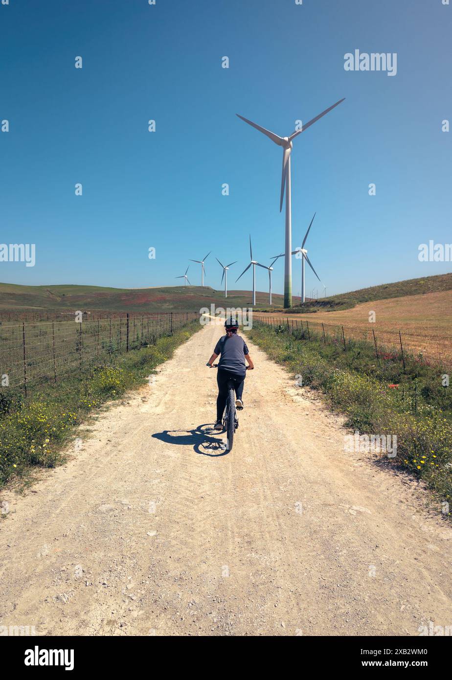 A person biking on a gravel path leading to impressive wind turbines ...